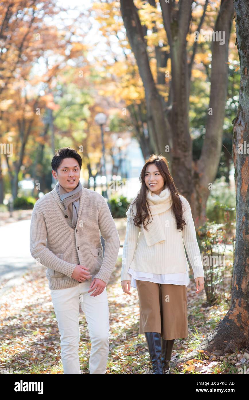 A couple in their 20s taking a walk along a tree-lined avenue in late ...