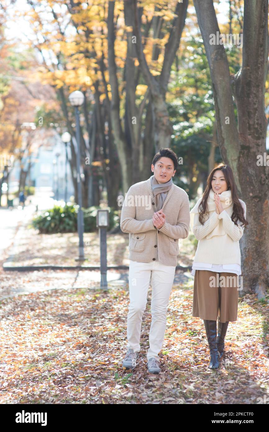 A couple in their 20s walking along a tree-lined avenue in late autumn ...