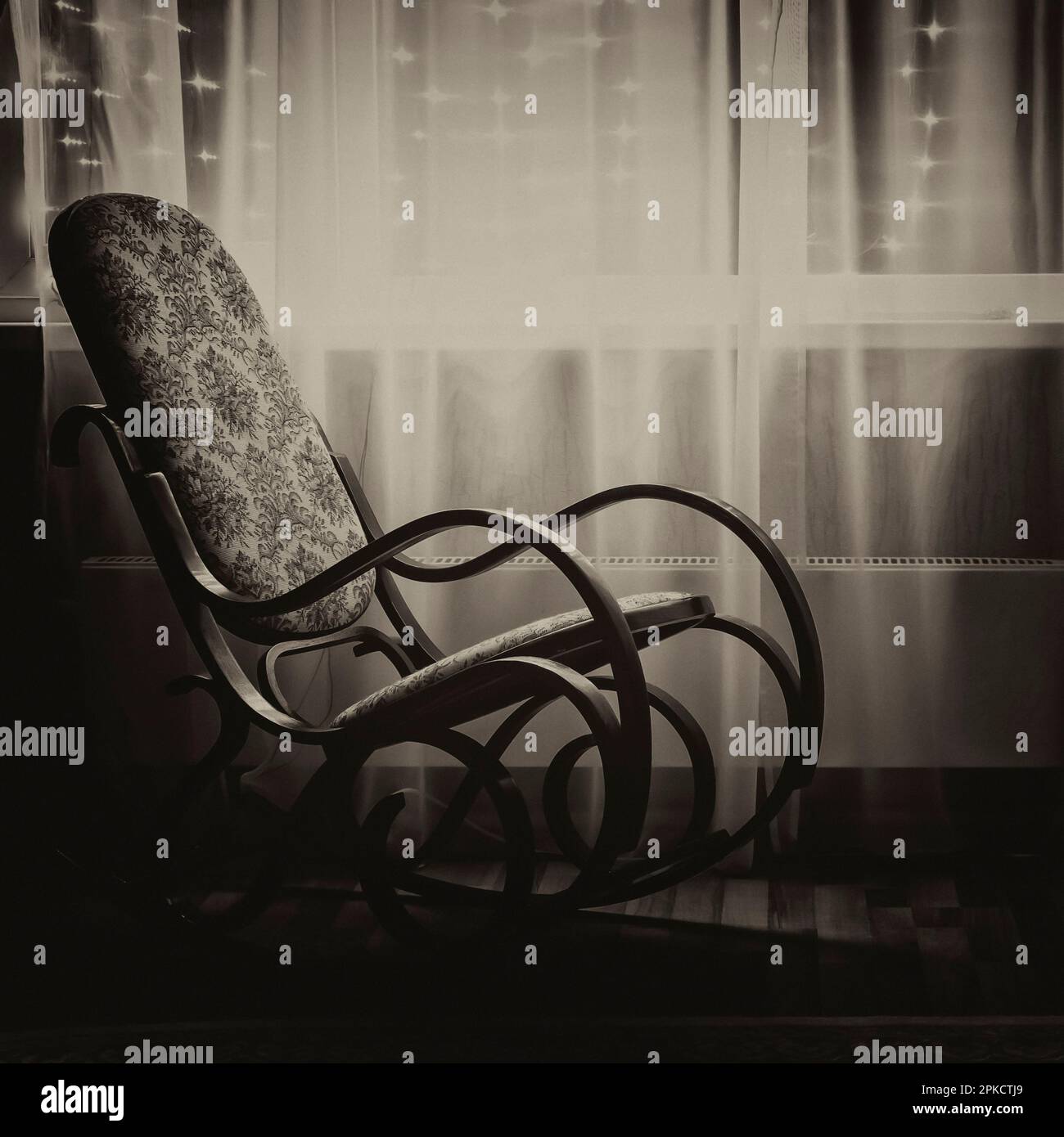 A rocking chair stands by the window in the evening light. Black and ...