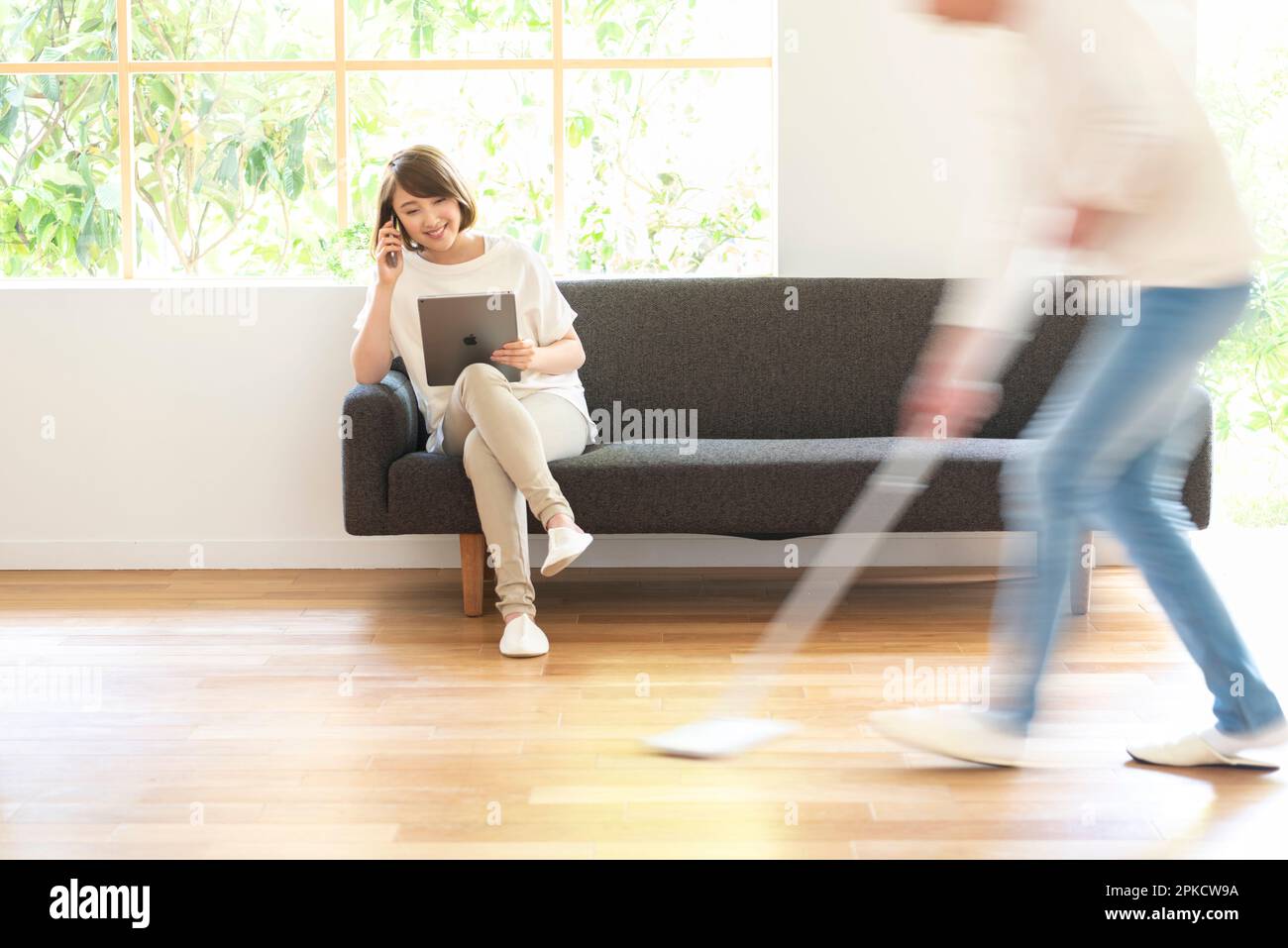 Woman in her 20s watching PC on the sofa with a cleaning man Stock ...