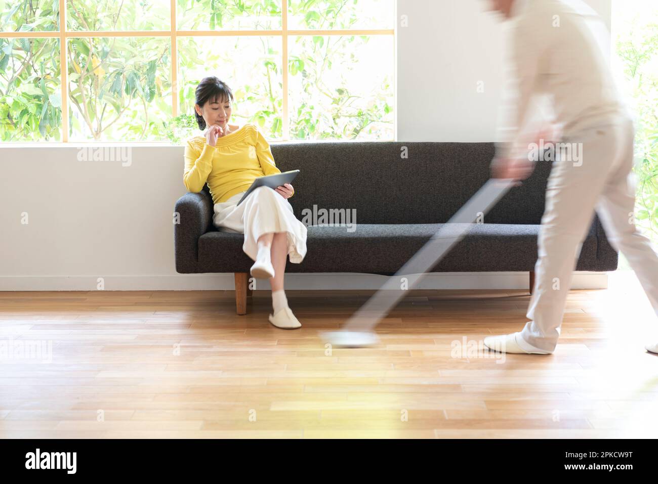 A middle-aged woman watching PC on the sofa with a cleaning man Stock ...