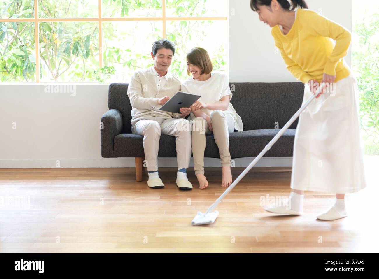 Father and daughter watching PC on the sofa with a cleaning woman Stock ...