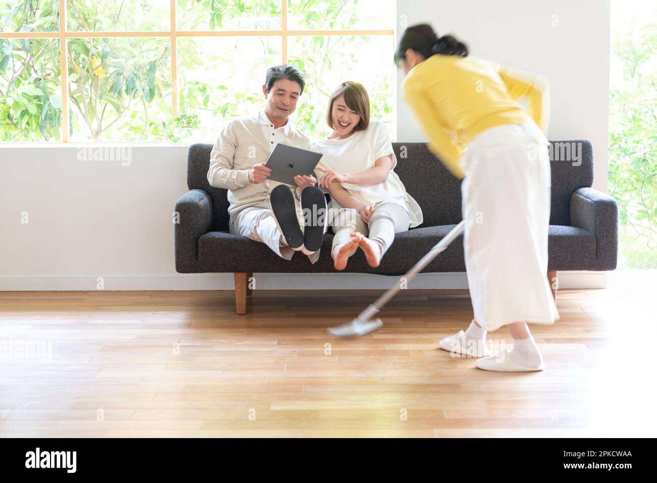 Father and daughter watching PC on the sofa with a cleaning woman Stock ...