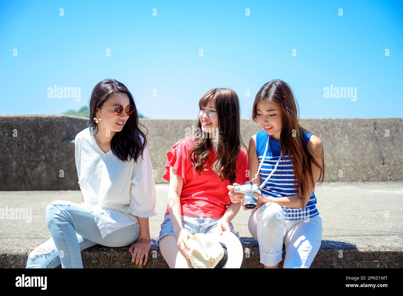 Three women traveling to a resort sitting on the sea breakwater Stock ...