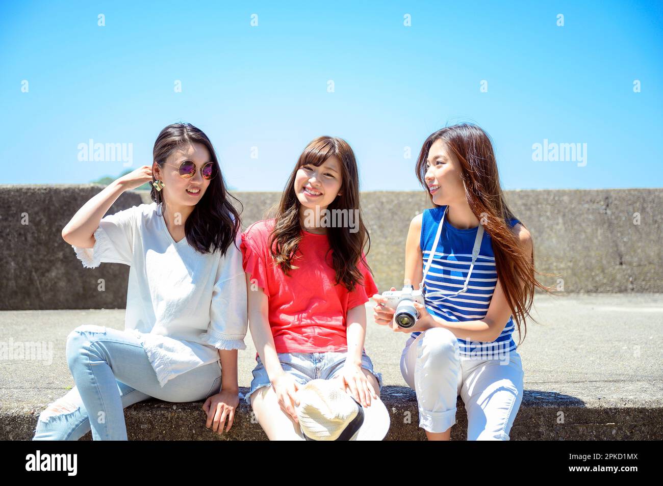 Three women traveling to a resort sitting on the sea breakwater Stock ...