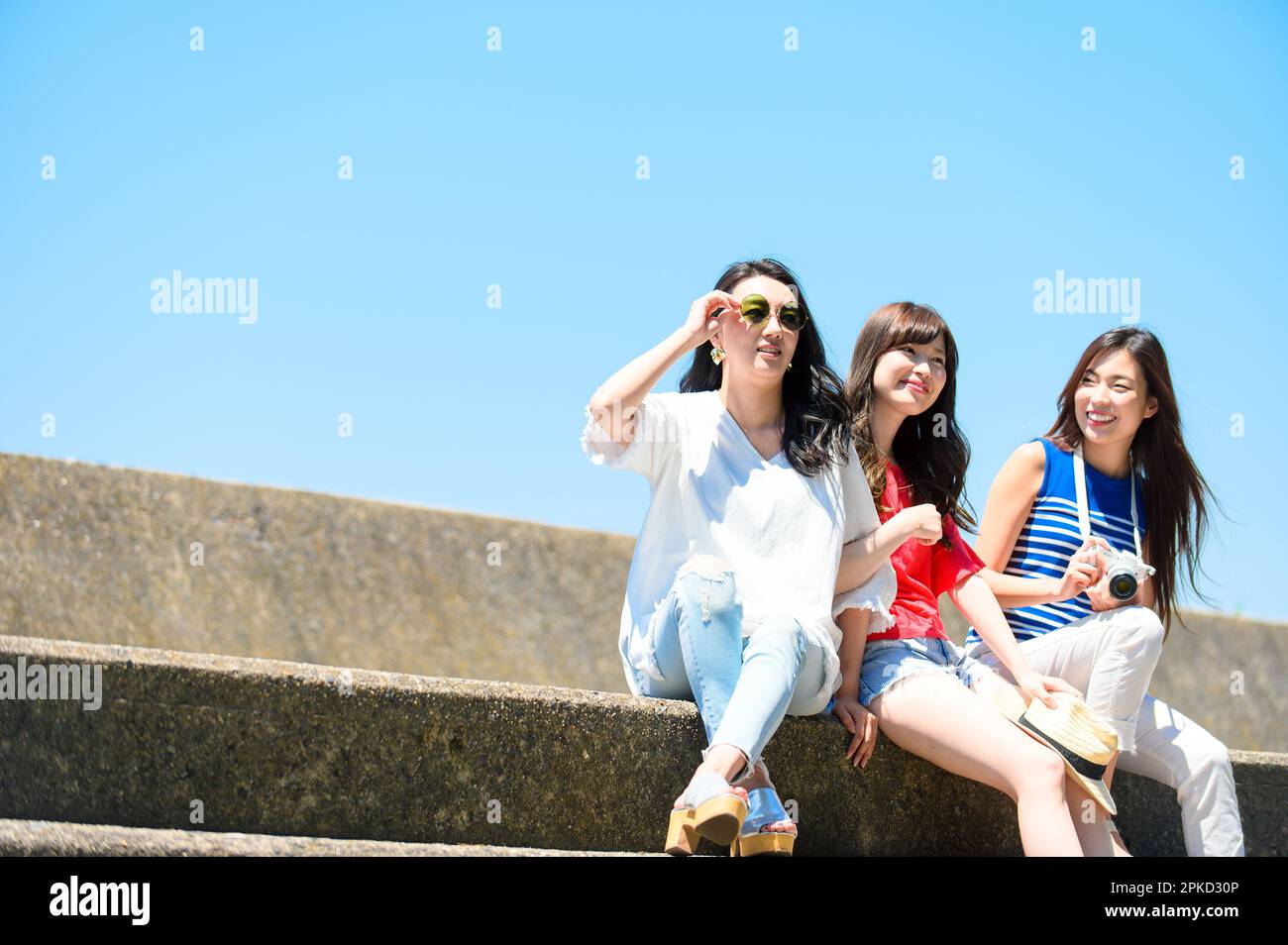 Three women traveling to a resort sitting on the sea breakwater Stock ...