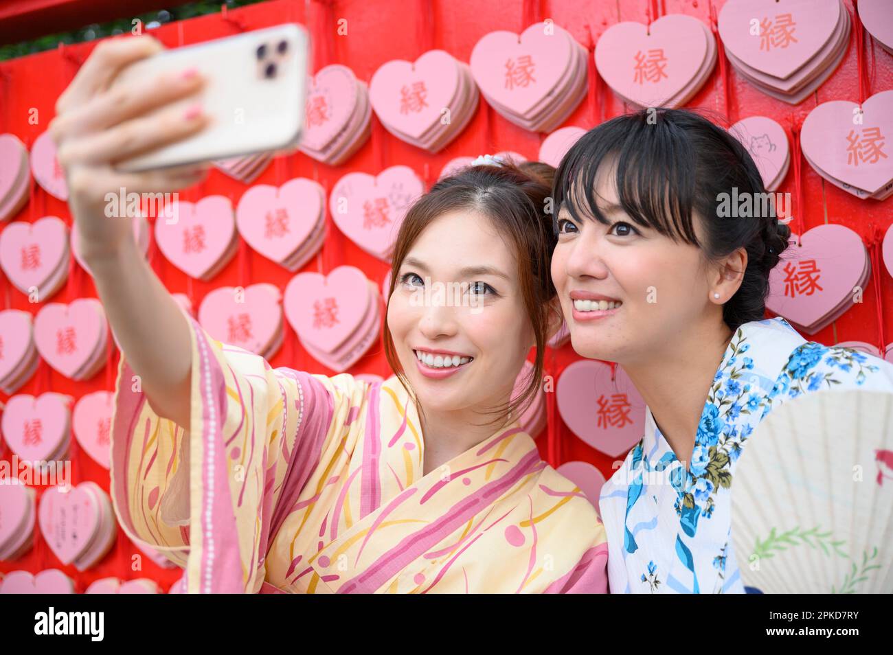 Two women in yukata praying for a match at a shrine and taking a ...