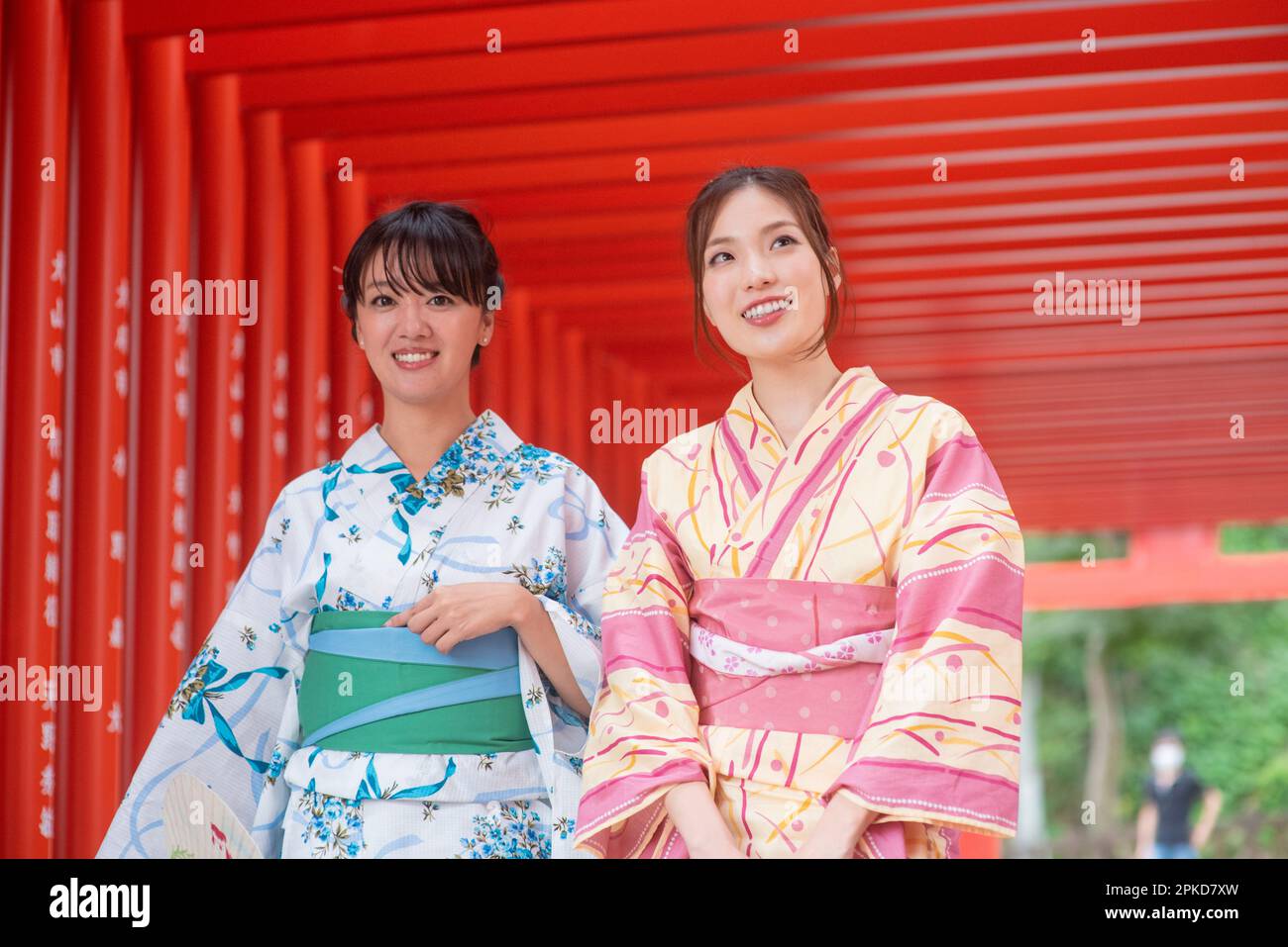 Two women in yukata passing through the torii gate of a Shinto shrine ...