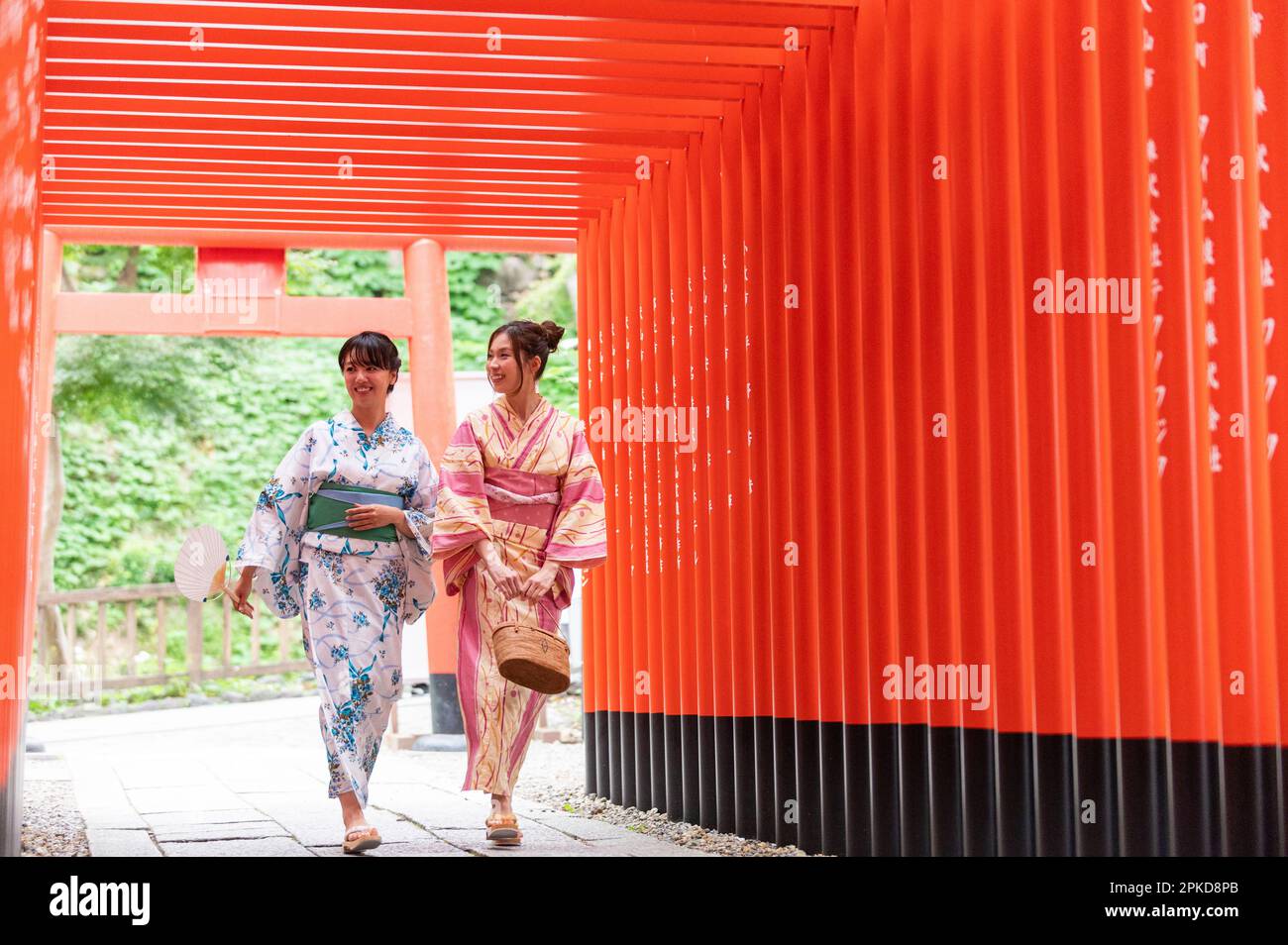 Two women in yukata walking through the torii gate of a Shinto shrine ...