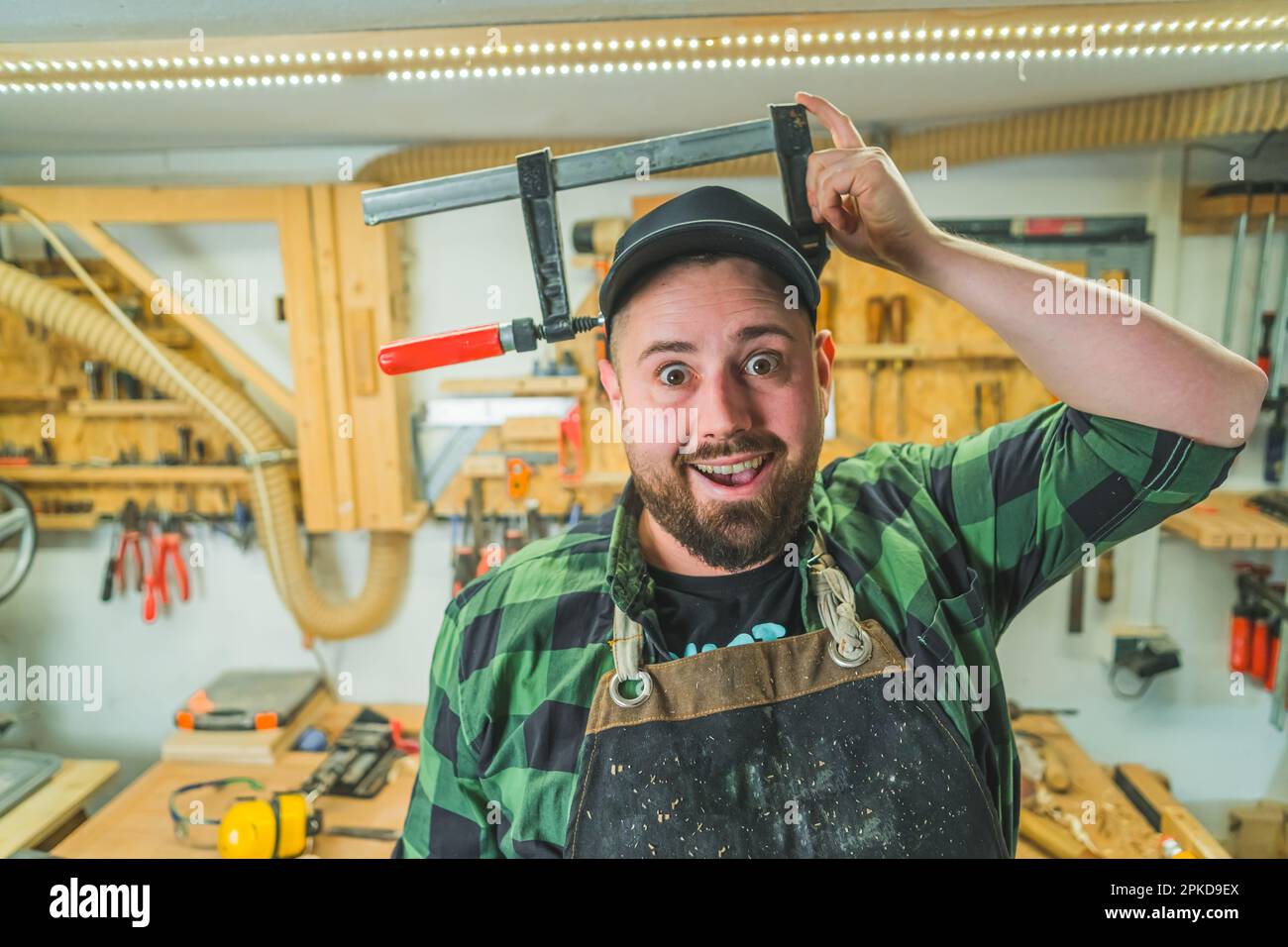 Funny positive male carpenter holding bar clamp on his head. Wood ...