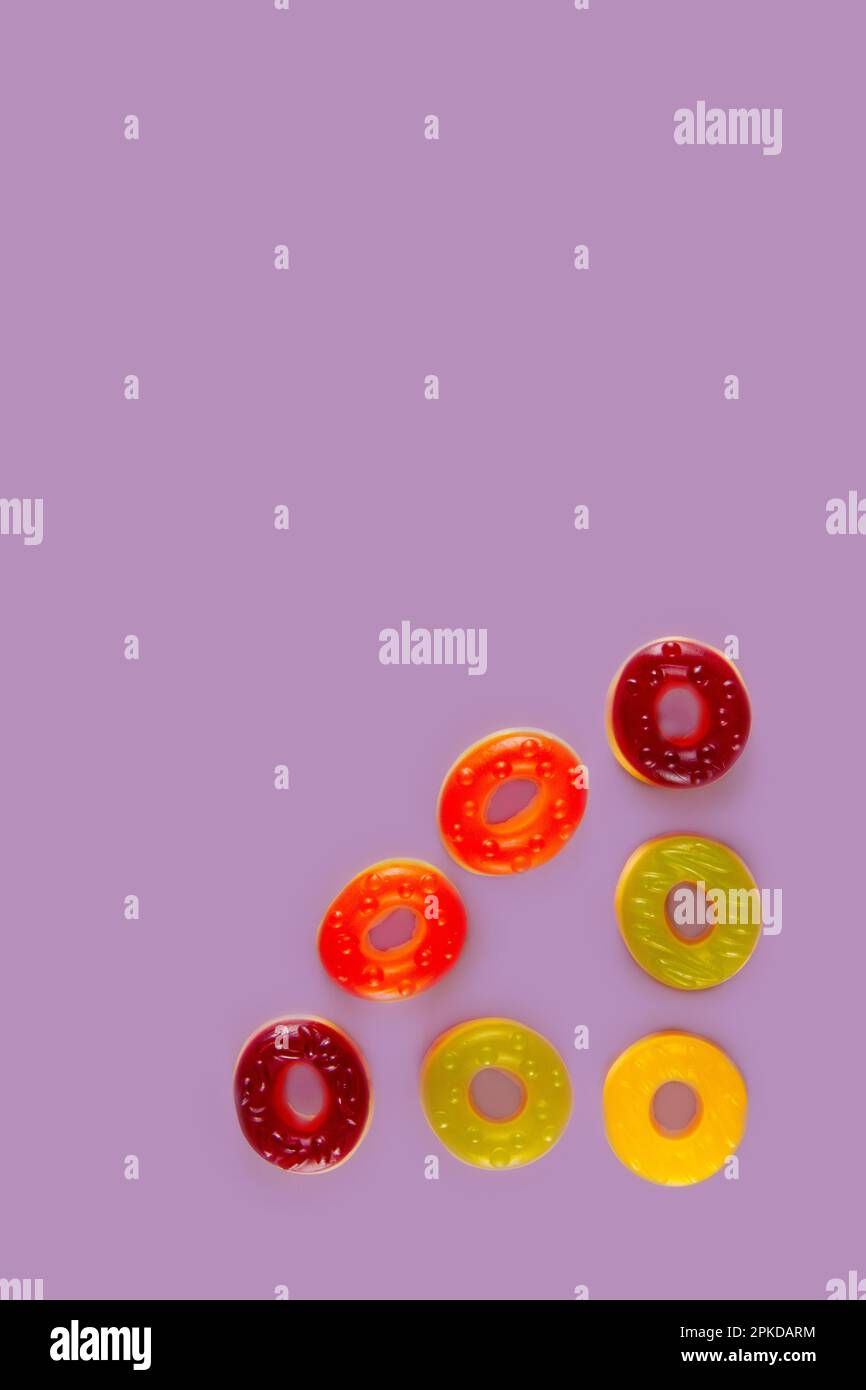 Triangle of round jelly candies at the corner of violet background ...