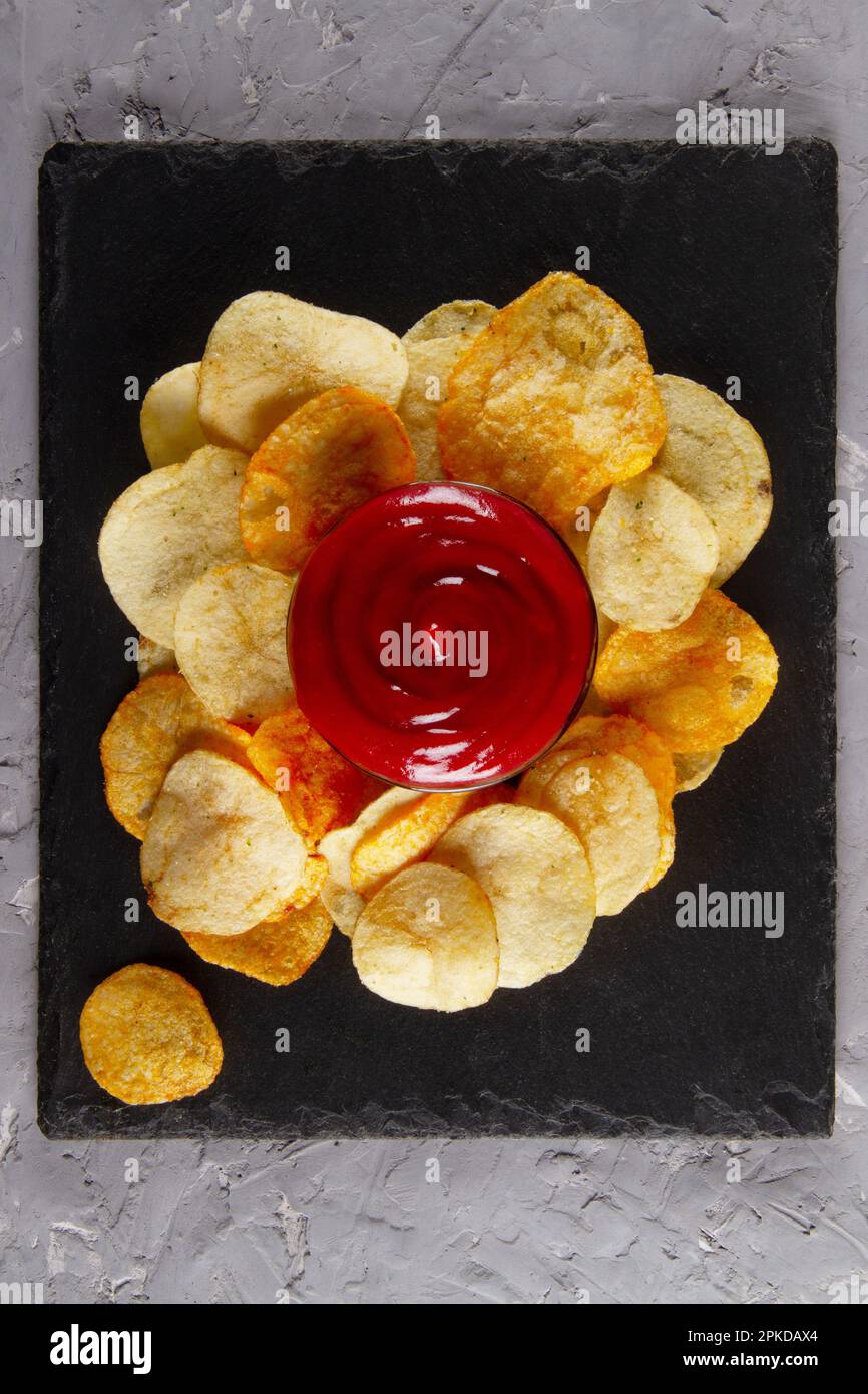 Top view of heap of potato chips with red dipping sauce on black slate ...