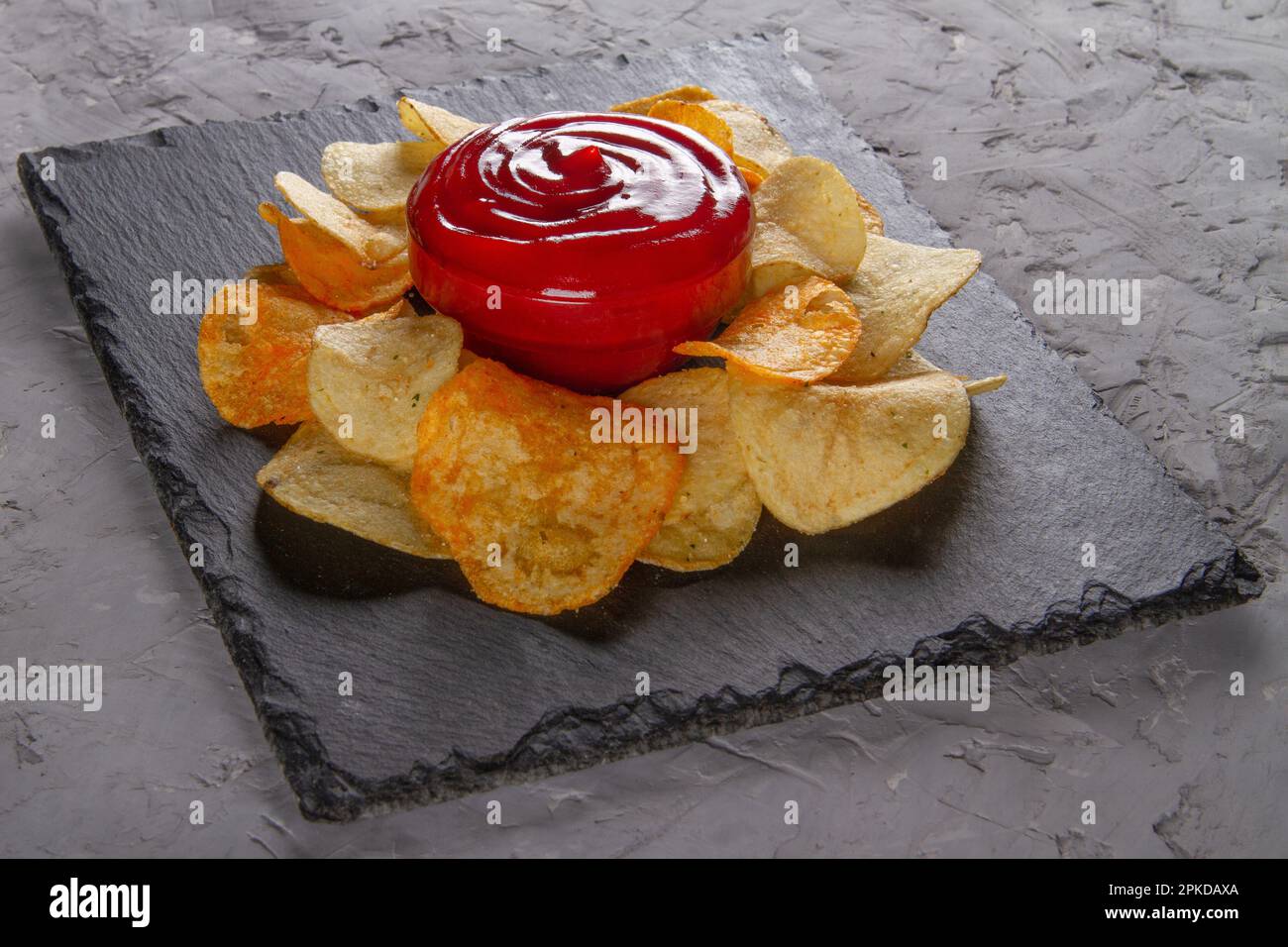 Side view of heap of potato chips with red dipping sauce on black slate ...