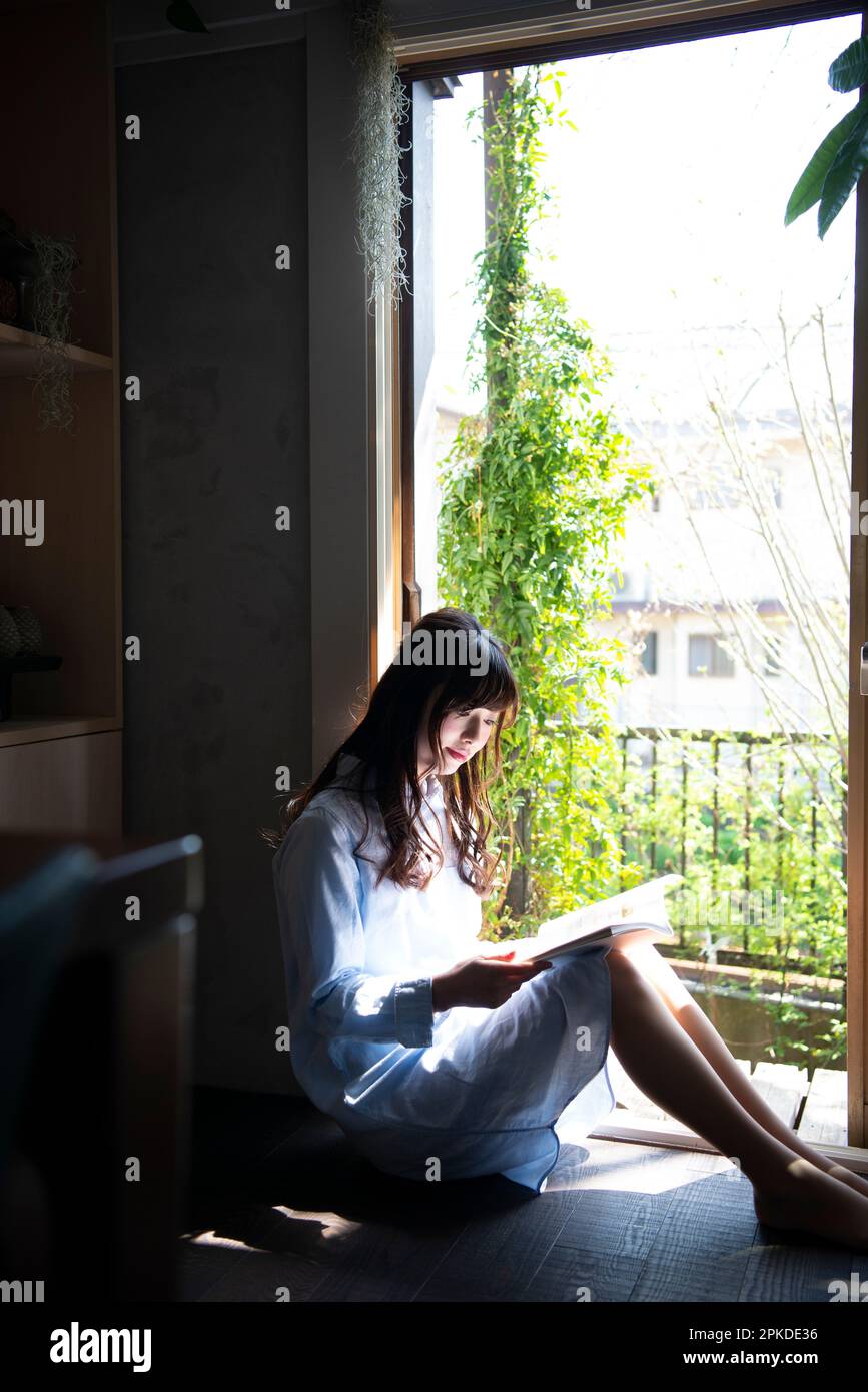 Woman sitting by the window reading a book Stock Photo - Alamy