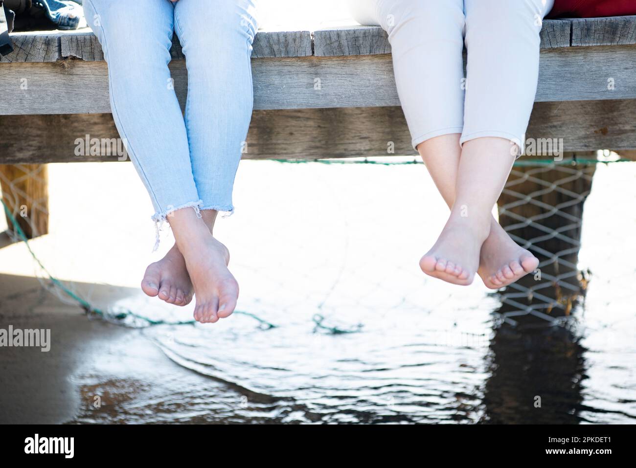 Legs of two women sitting on a pier Stock Photo - Alamy