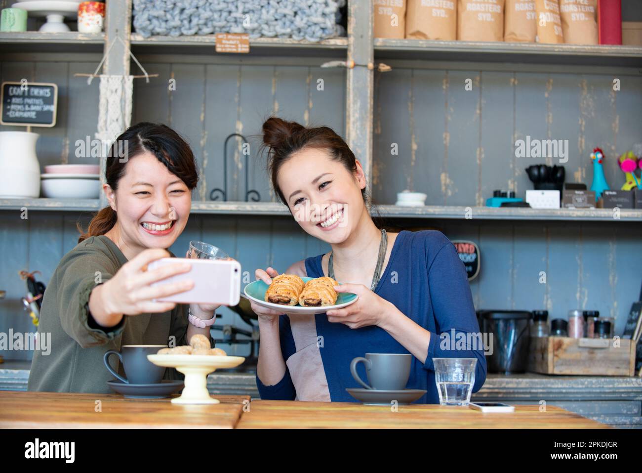 Women taking selfies with sweets using their smartphones at a café ...