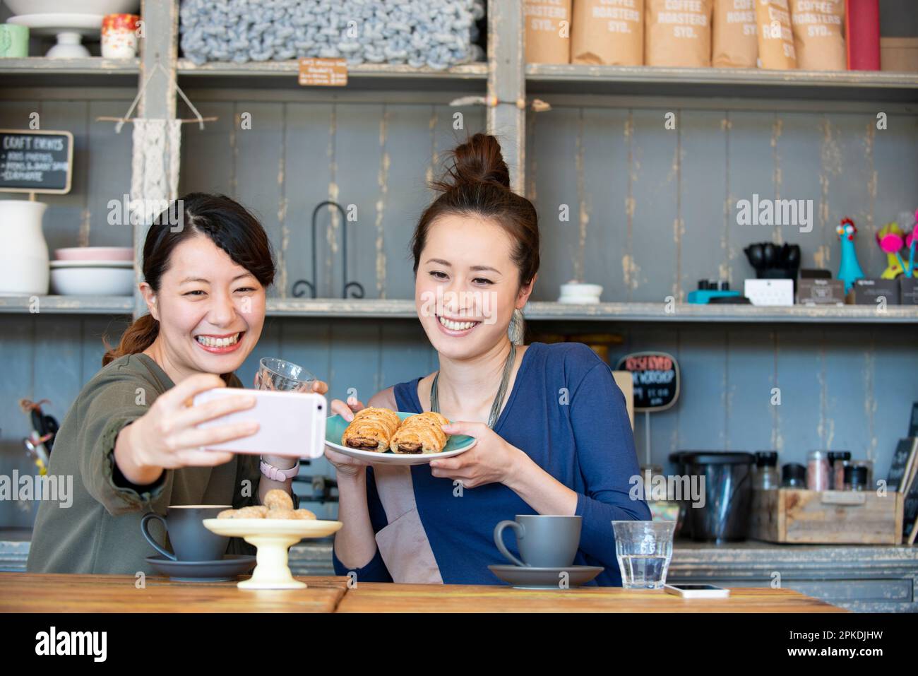 Women taking selfies with sweets using their smartphones at a café ...