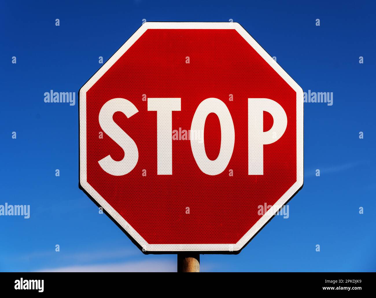 A red octagonal stop sign mounted on a metal post with a blue sky ...