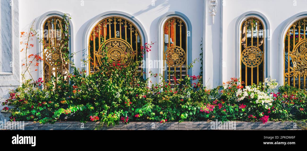 A white building with gold gate red yellow flowers background green ...
