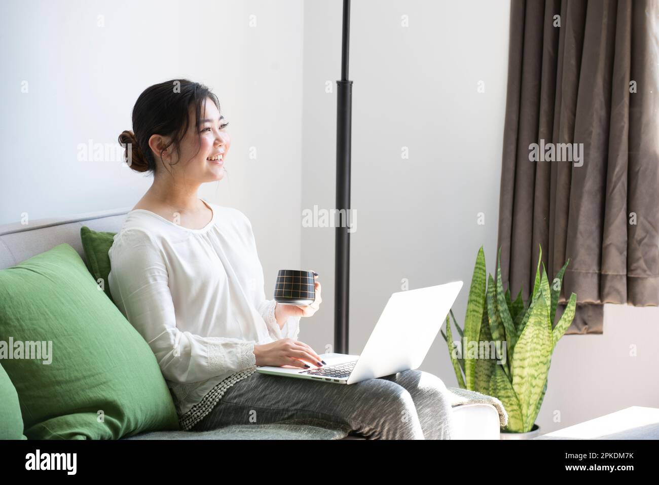 Woman laughing while operating a computer on a sofa Stock Photo - Alamy