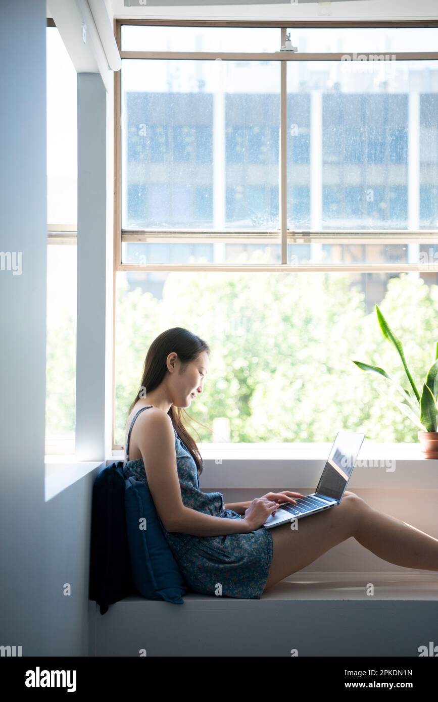 Woman sitting on window sill touching computer Stock Photo - Alamy