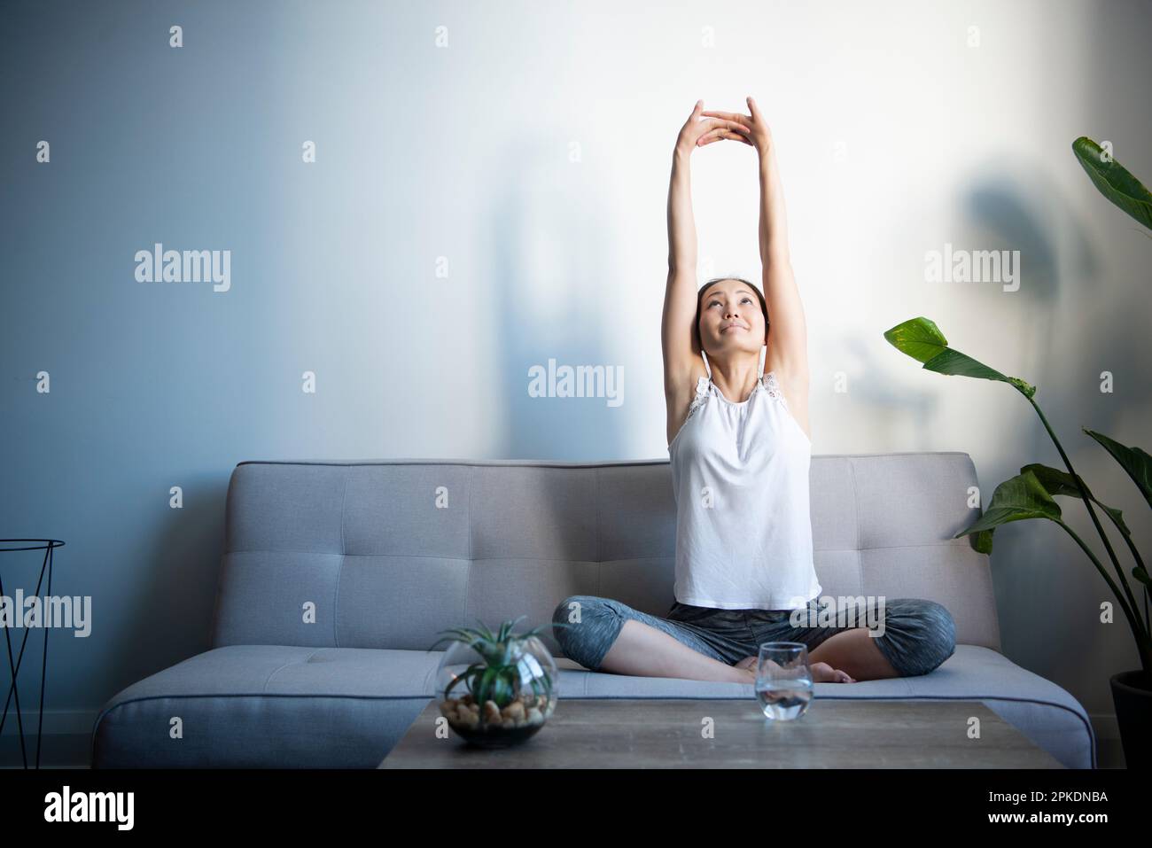 Woman sitting and stretching on living room sofa Stock Photo - Alamy