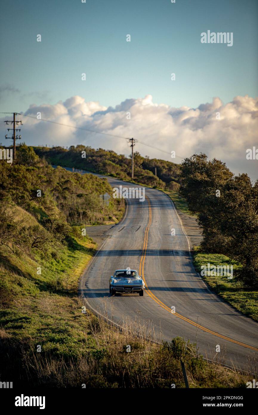 A car driving on a road with a scenic cloud backdrop in the background ...