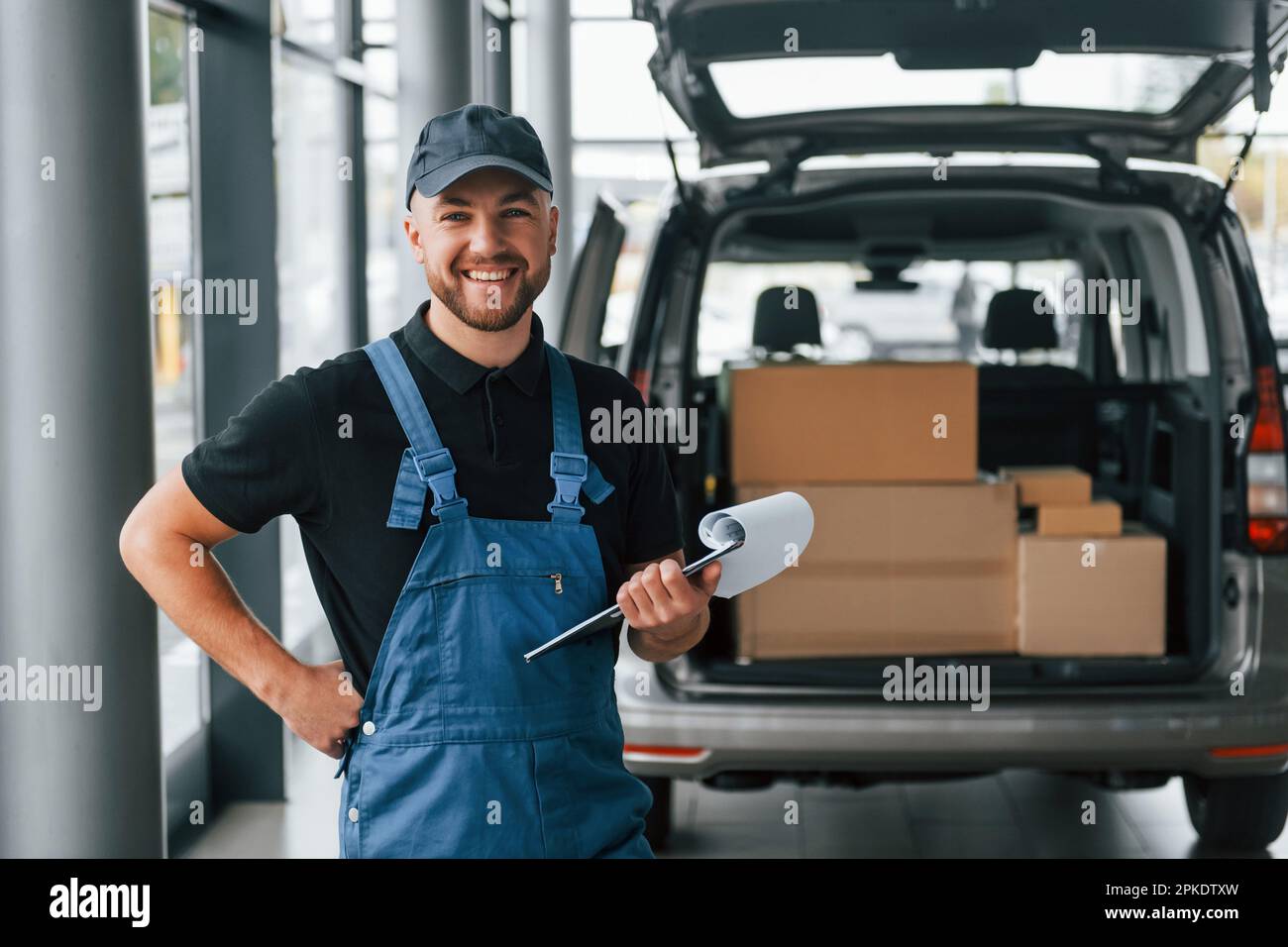 With document. Delivery man in uniform is indoors with car and with ...