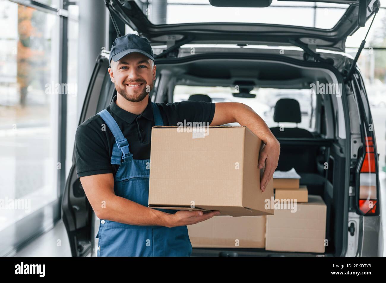 Holding box. Delivery man in uniform is indoors with car and with order ...