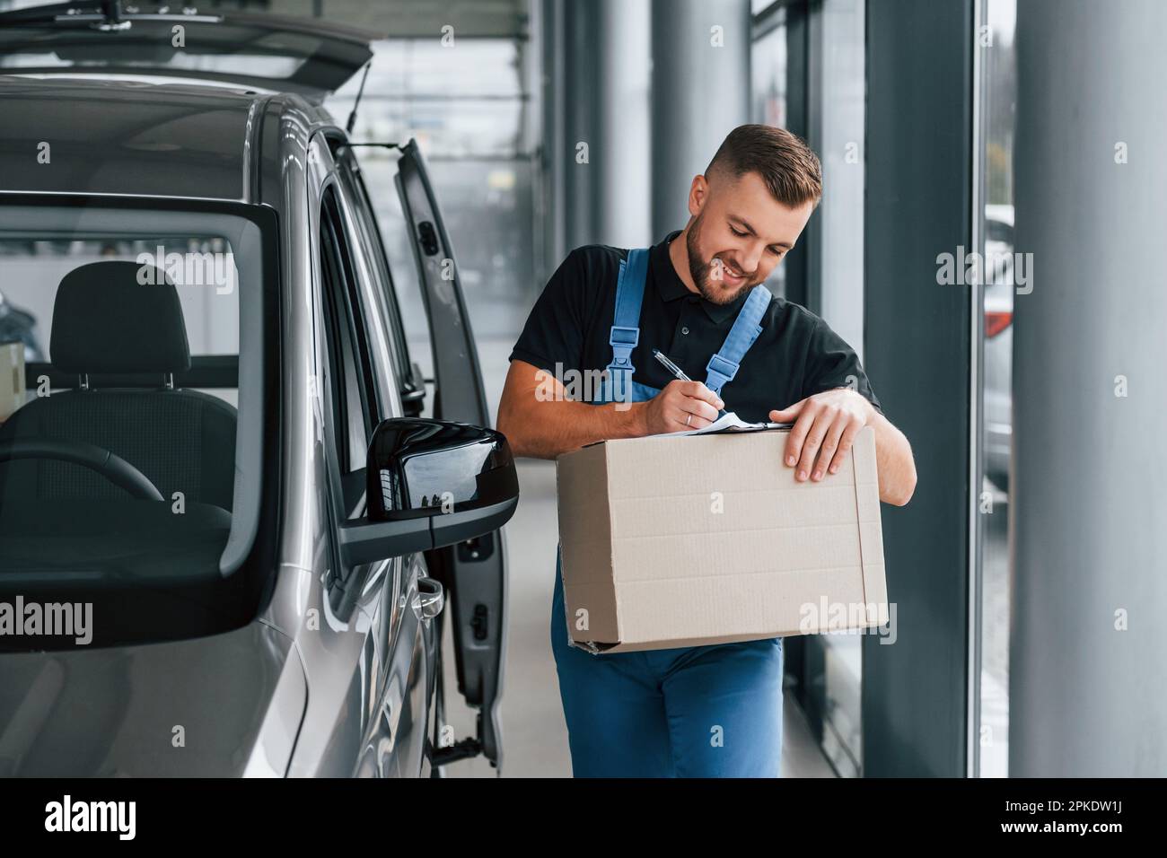 Paper box. Delivery man in uniform is indoors with car and with order ...