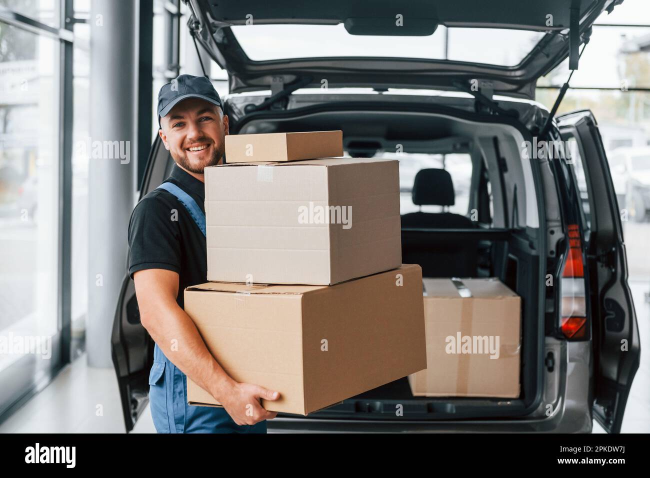 Three boxes. Delivery man in uniform is indoors with car and with order ...