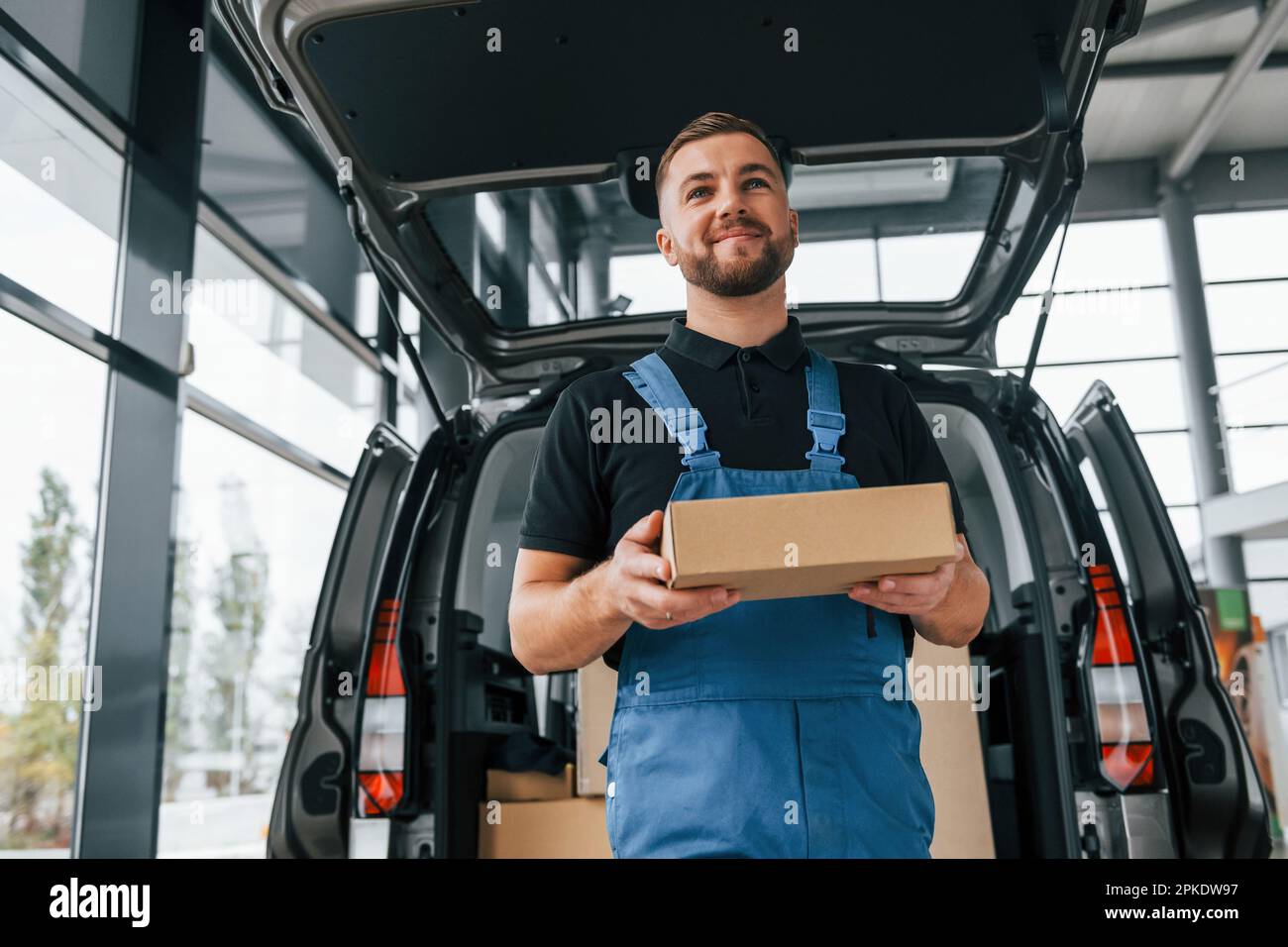 Front view. Delivery man in uniform is indoors with car and with order ...
