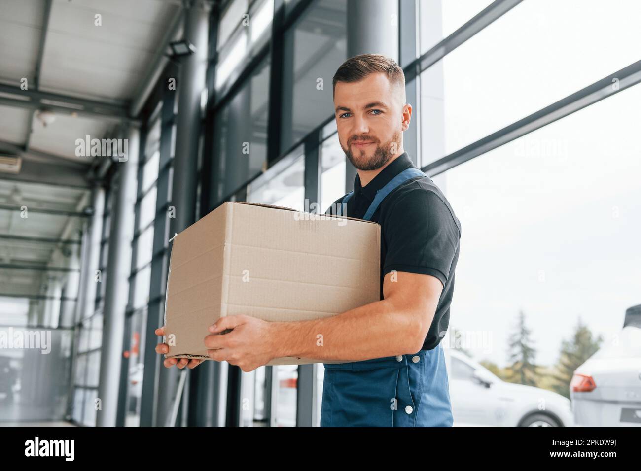 Front view. Delivery man in uniform is indoors with car and with order ...