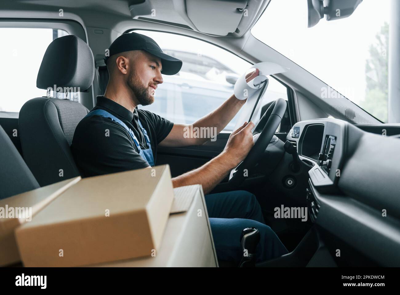 With vehicle. Delivery man in uniform is indoors with car and with ...