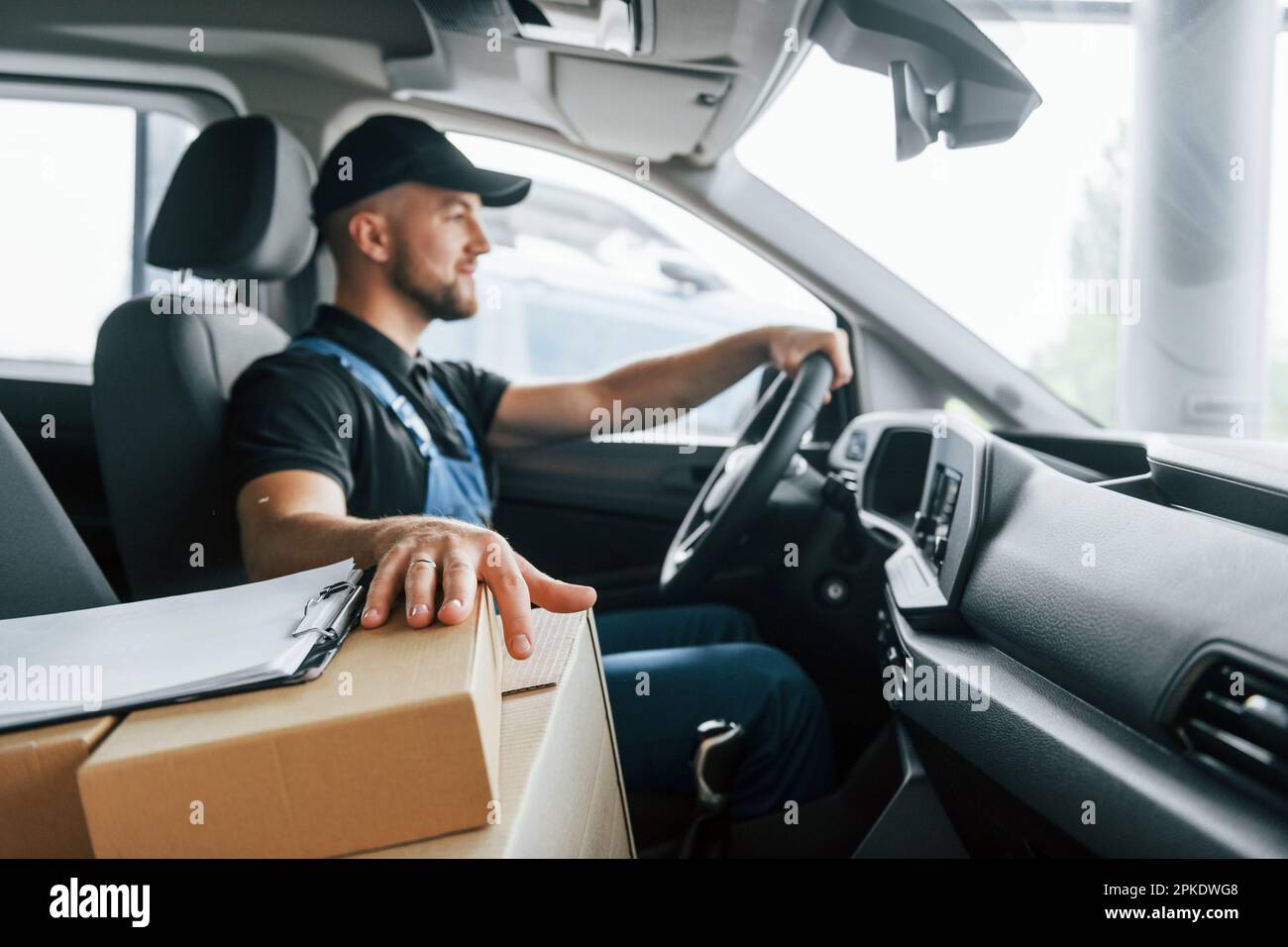 Modern vehicle. Delivery man in uniform is indoors with car and with ...