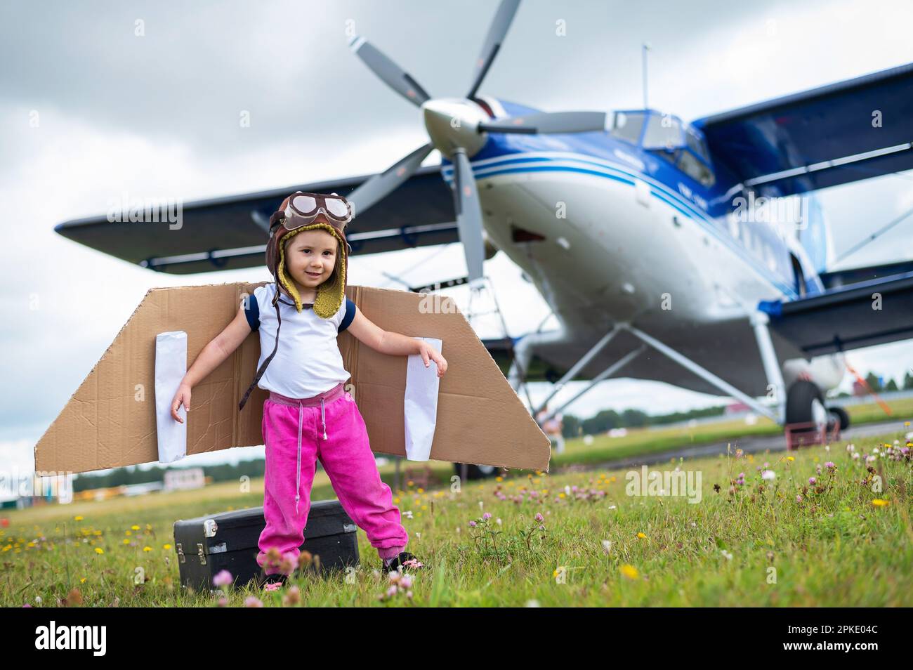 A little girl in a pilot's costume with cardboard wings runs on the ...