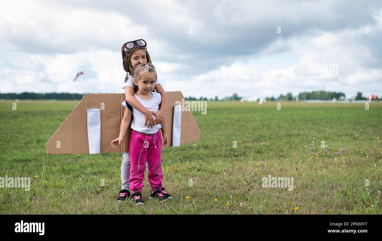 Little girls in a pilot's costume are hugging outdoors. Two sisters ...