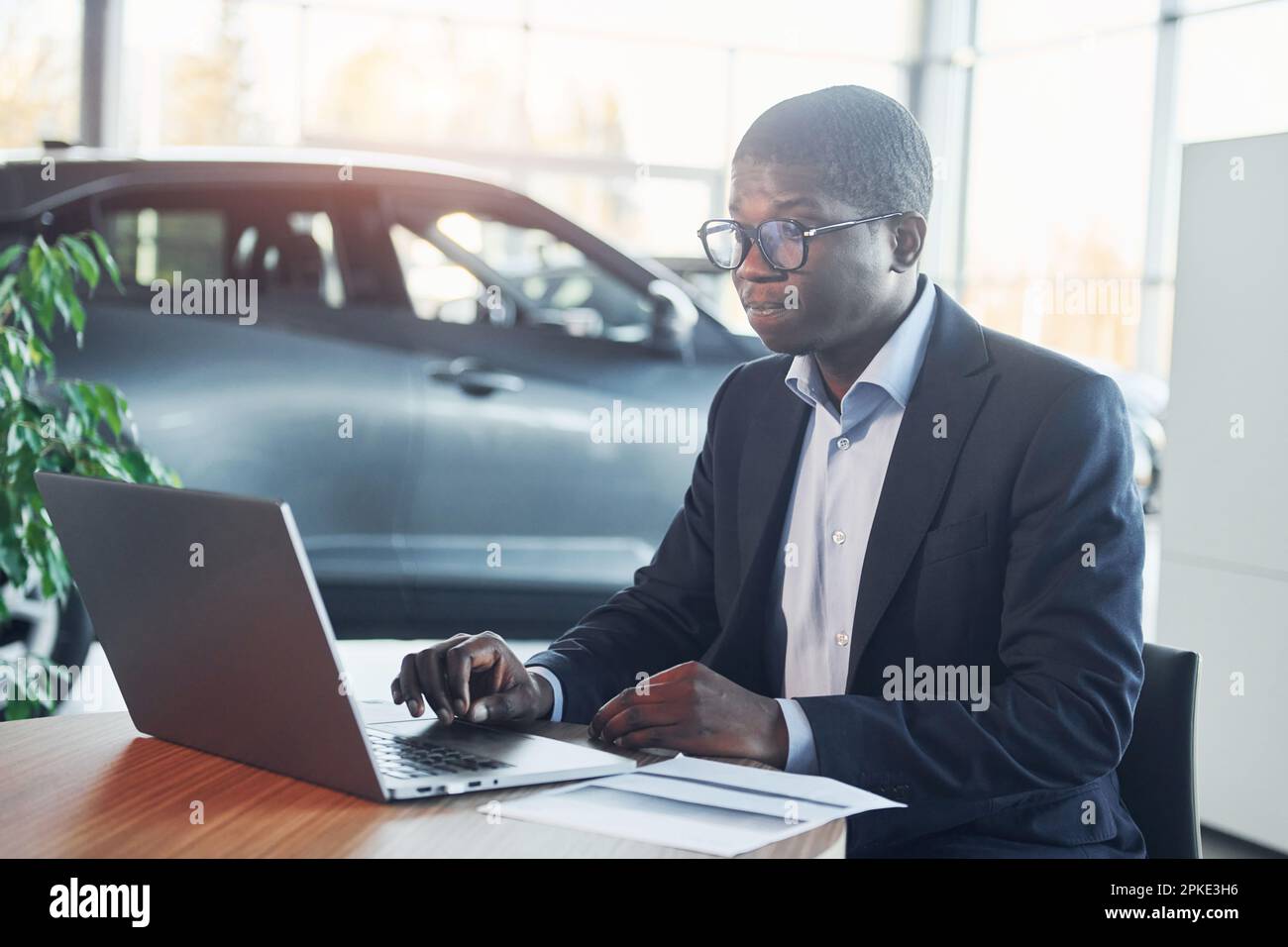 Office worker is sitting in autosalon by table with laptop Stock Photo ...