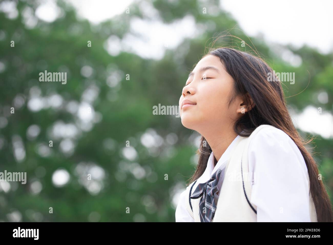 Schoolgirl in school uniform taking a deep breath with her eyes closed ...
