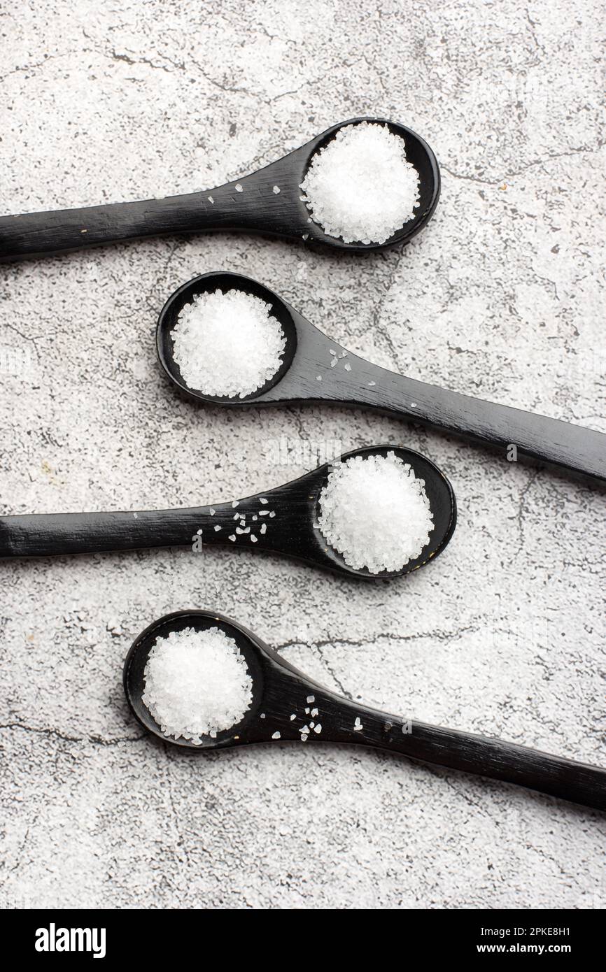 Salt on four black spoons on a gray stone kitchen counter in a top view ...