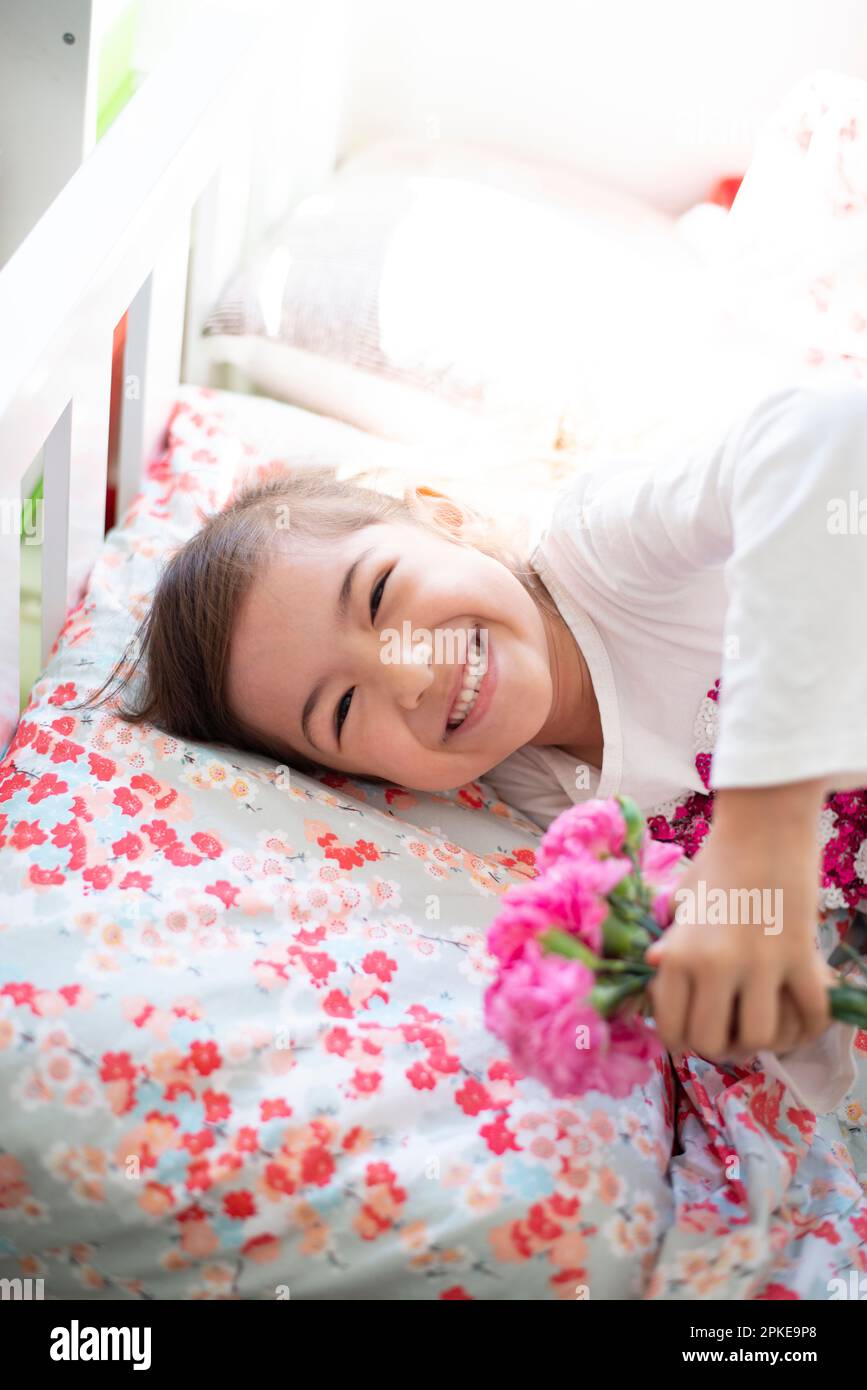 Girl lying on bed holding carnation Stock Photo - Alamy