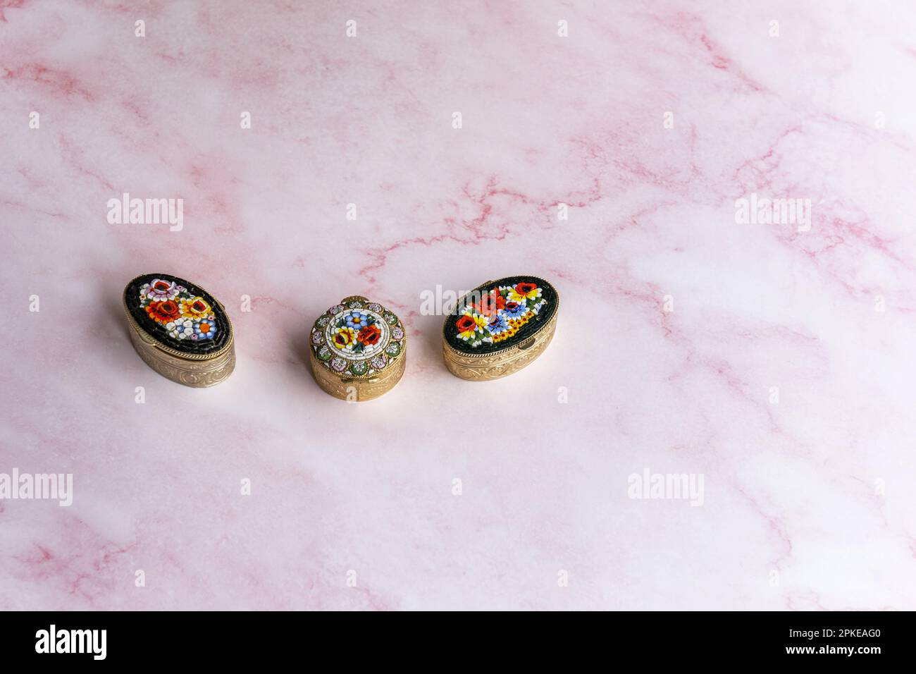 Three small decorative boxes or pillboxes in gold metal on a pink ...