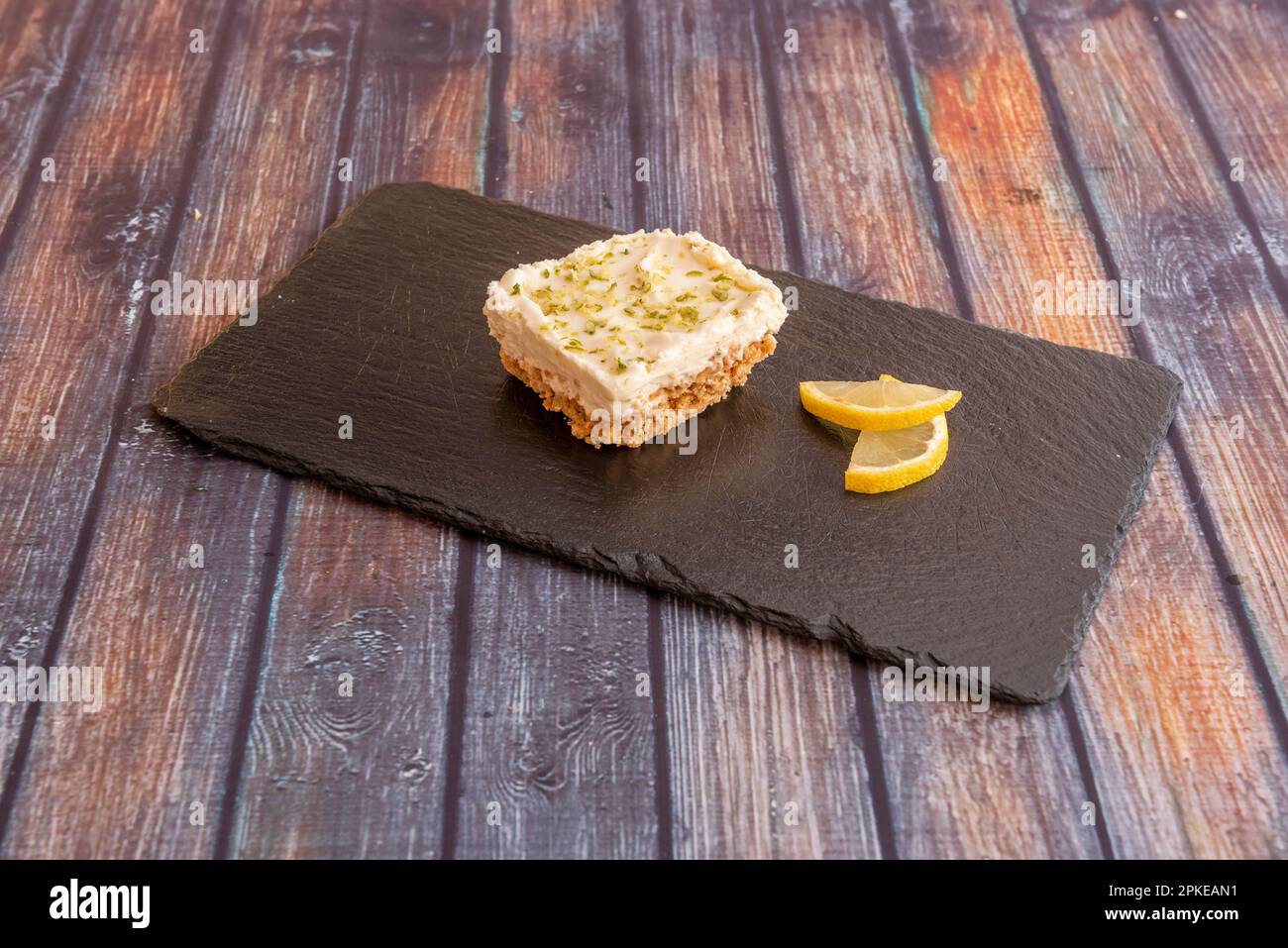 A slice of lemon tart with a biscuit base on a black slate tray Stock ...