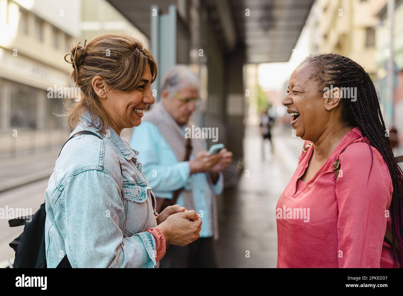 Happy multiracial women friends talking while waiting at the bus ...