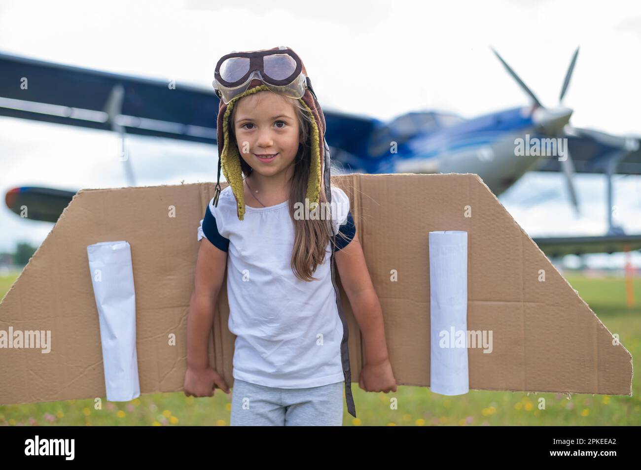A little girl in a pilot's costume with cardboard wings runs on the ...