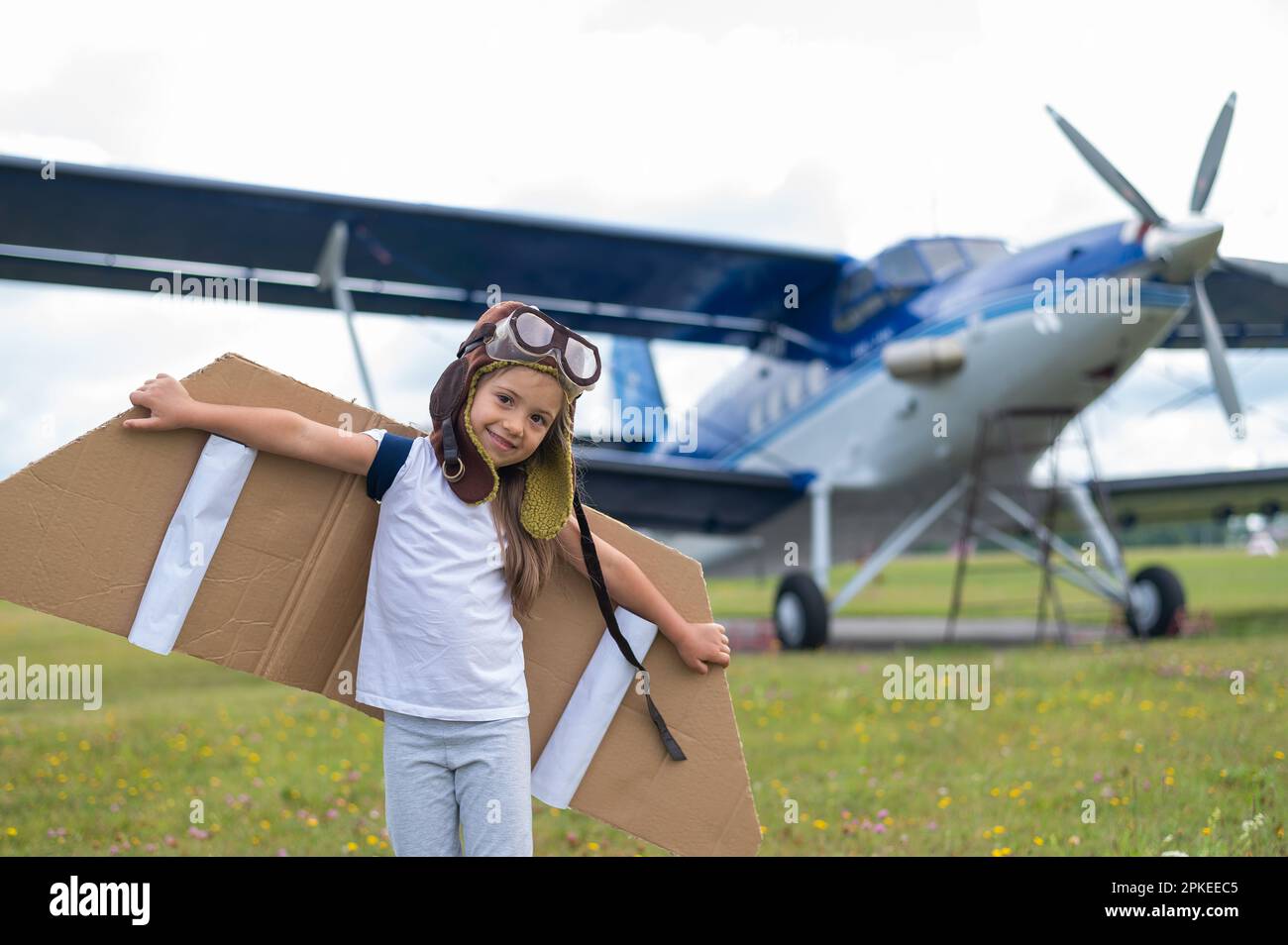A little girl plays a pilot on the background of a small plane with a ...