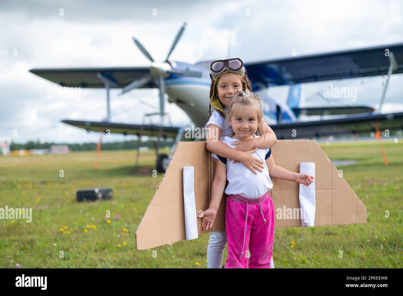 Two little girls in pilot's costumes are hugging in the field by the ...