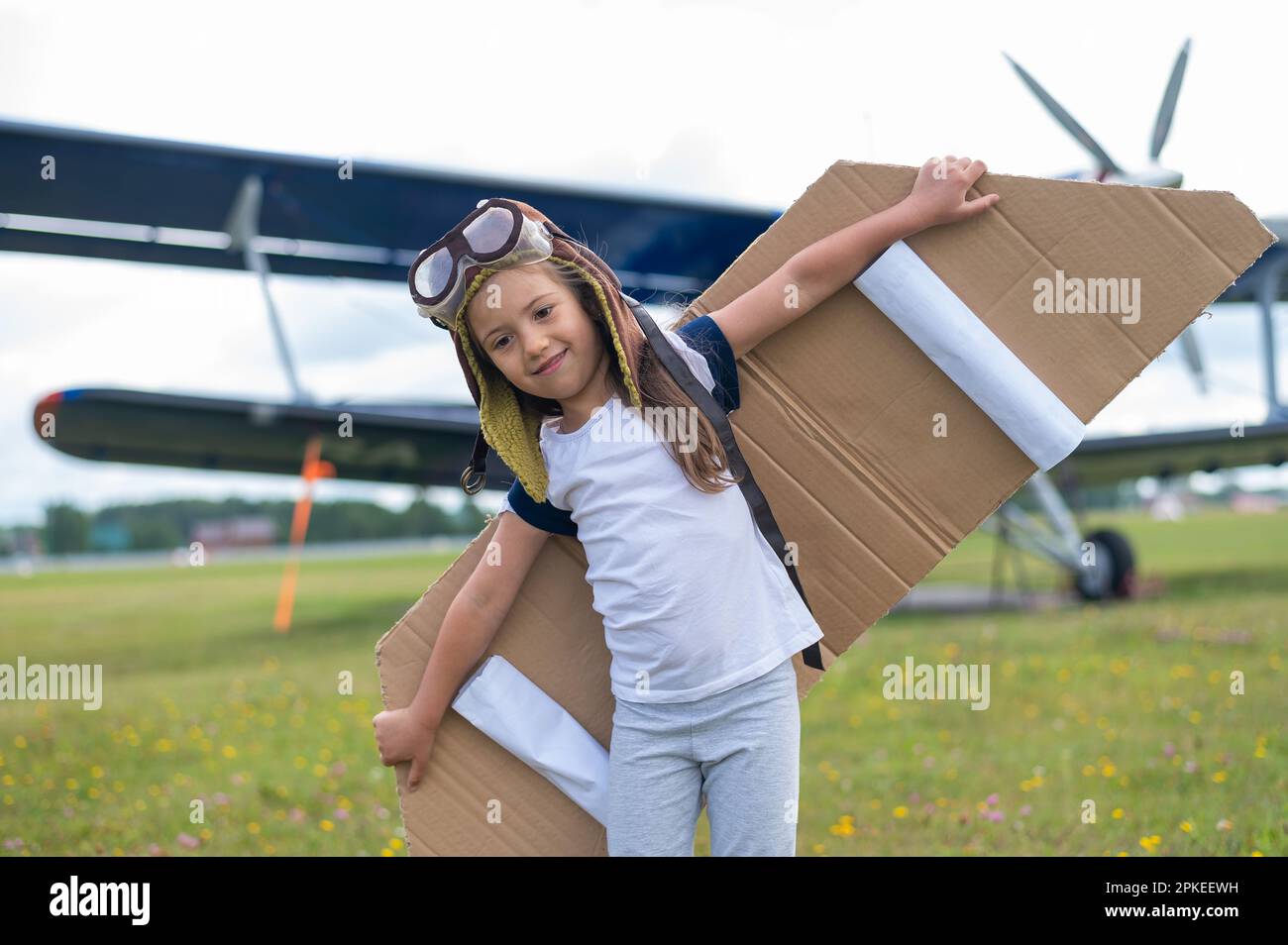 A little girl plays a pilot on the background of a small plane with a ...