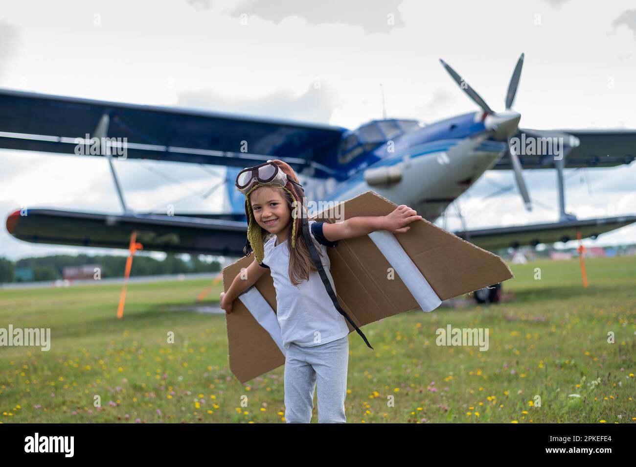A little girl plays a pilot on the background of a small plane with a ...