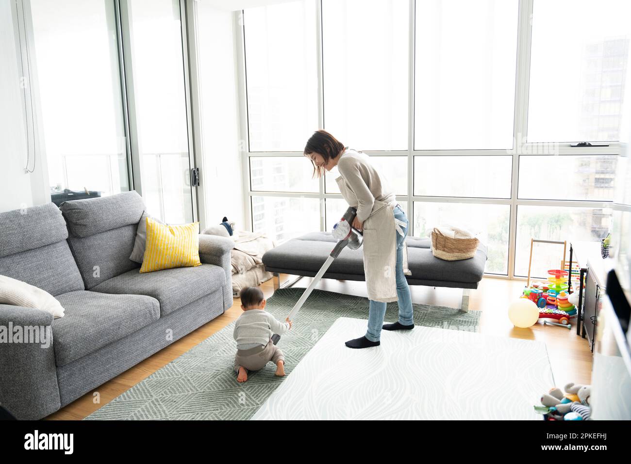 Mother vacuuming at home with baby by her side Stock Photo - Alamy